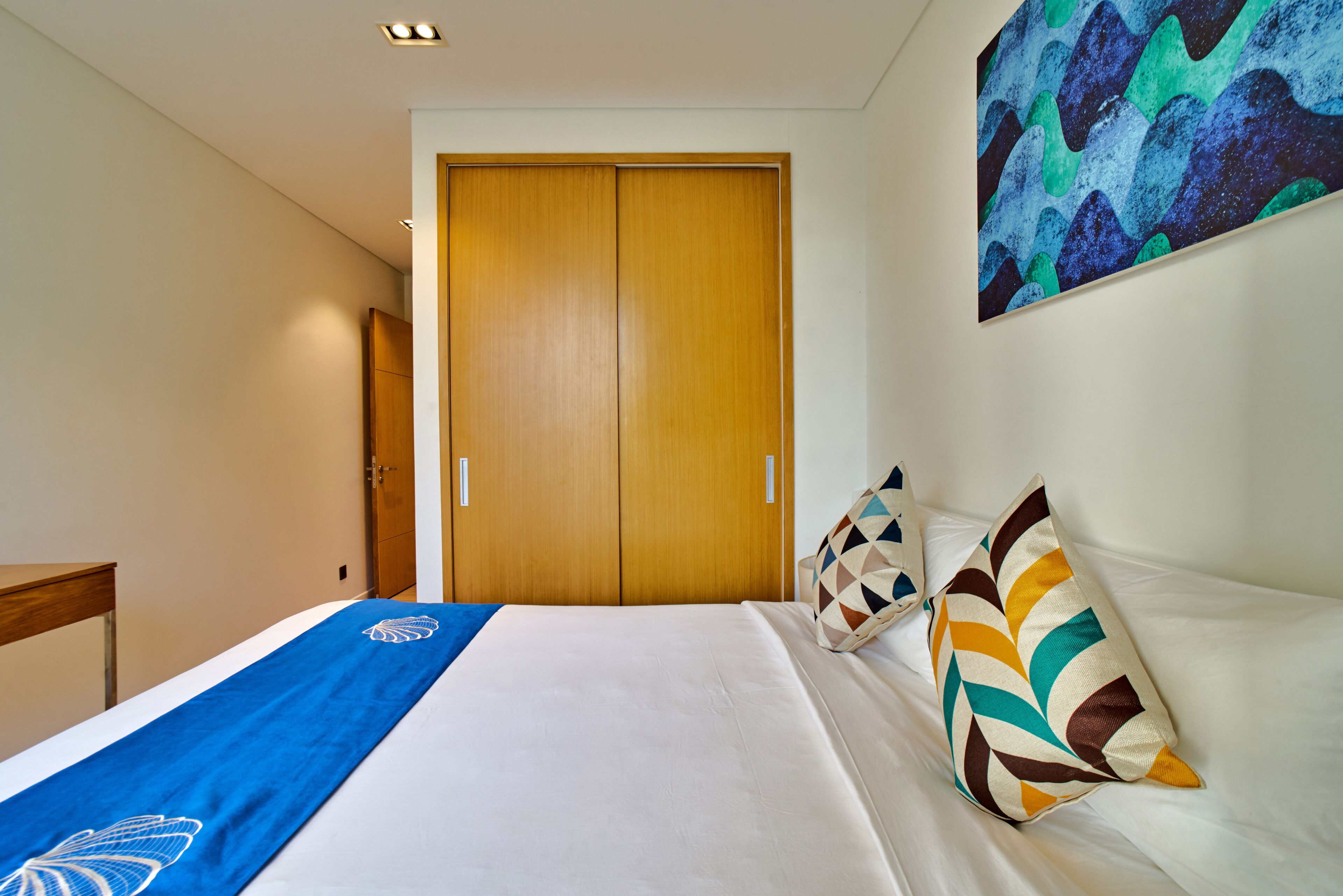 Quarto de hotel com uma cama, um guarda-roupa de madeira, um quadro na parede e uma toalha azul sobre a cama.