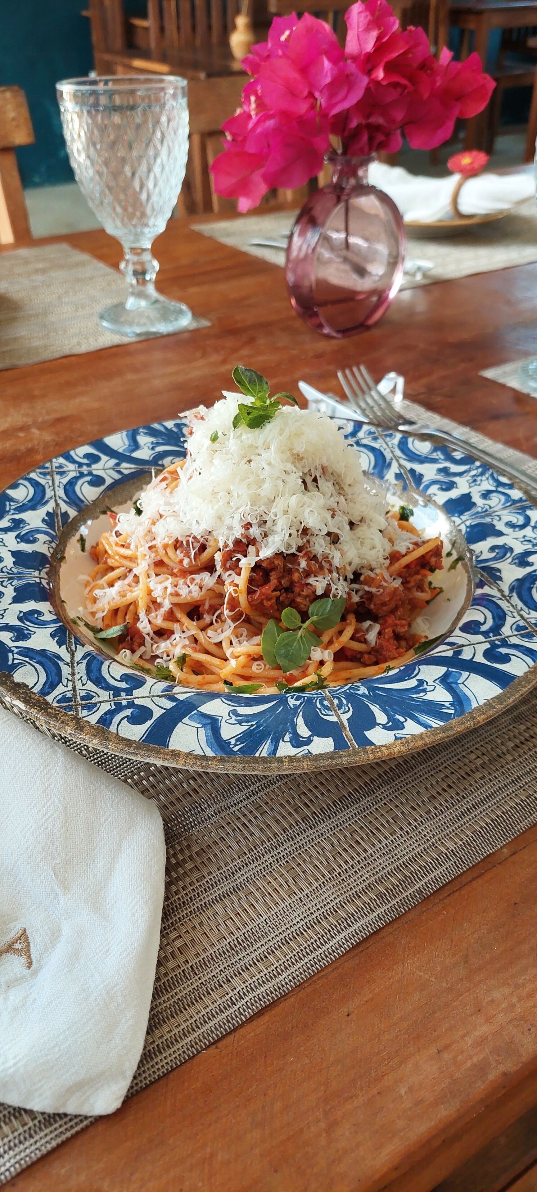 Um prato de espaguete com molho de carne e queijo ralado, servido em um prato com padrão azul e branco.
