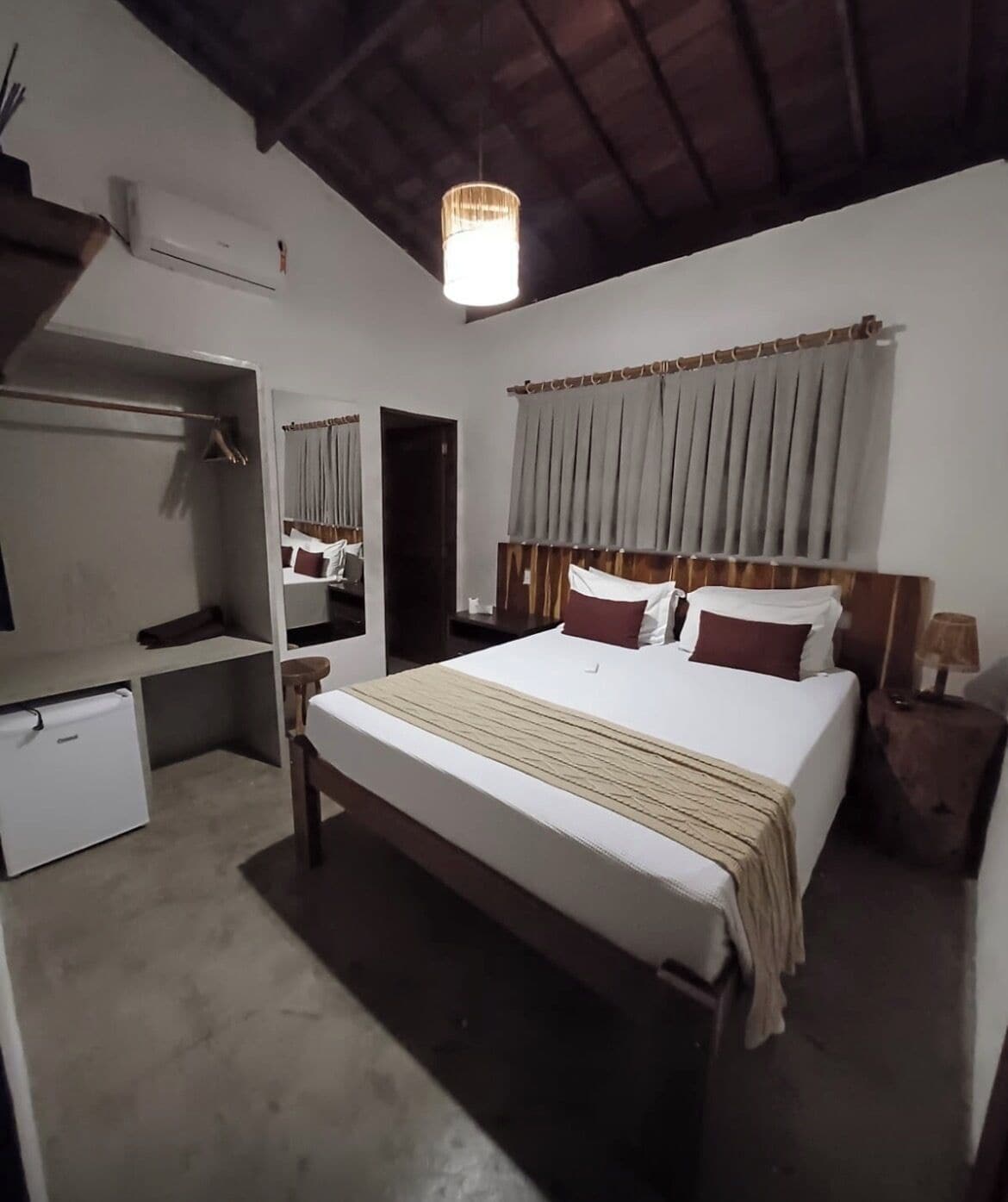 Quarto com cama, mesa de cabeceira, luminária, guarda-roupa, espelho e aparelho de ar condicionado.