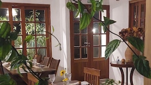 Uma área de refeições com móveis de madeira, uma mesa com um vaso de flores e um cesto no chão.