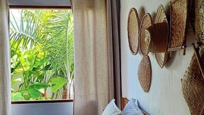Quarto com cama, almofadas e vista para o verde pela janela.