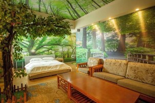 Quarto com cama, sofá, mesa de centro e um mural com paisagem de floresta.