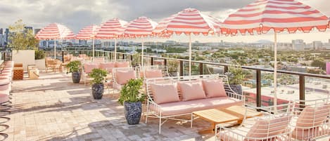 Terraço no topo com guarda-sóis listrados, áreas de estar e plantas em vasos.
