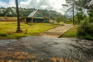 Uma casa com telhado inclinado, varanda coberta e um pequeno riacho na frente.