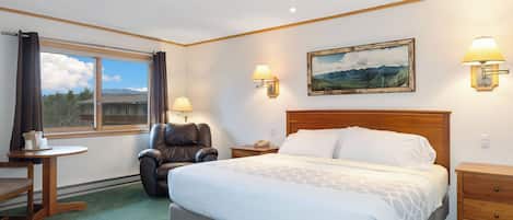 Quarto de hotel com uma cama grande, uma cadeira, uma mesa pequena e um quadro na parede.