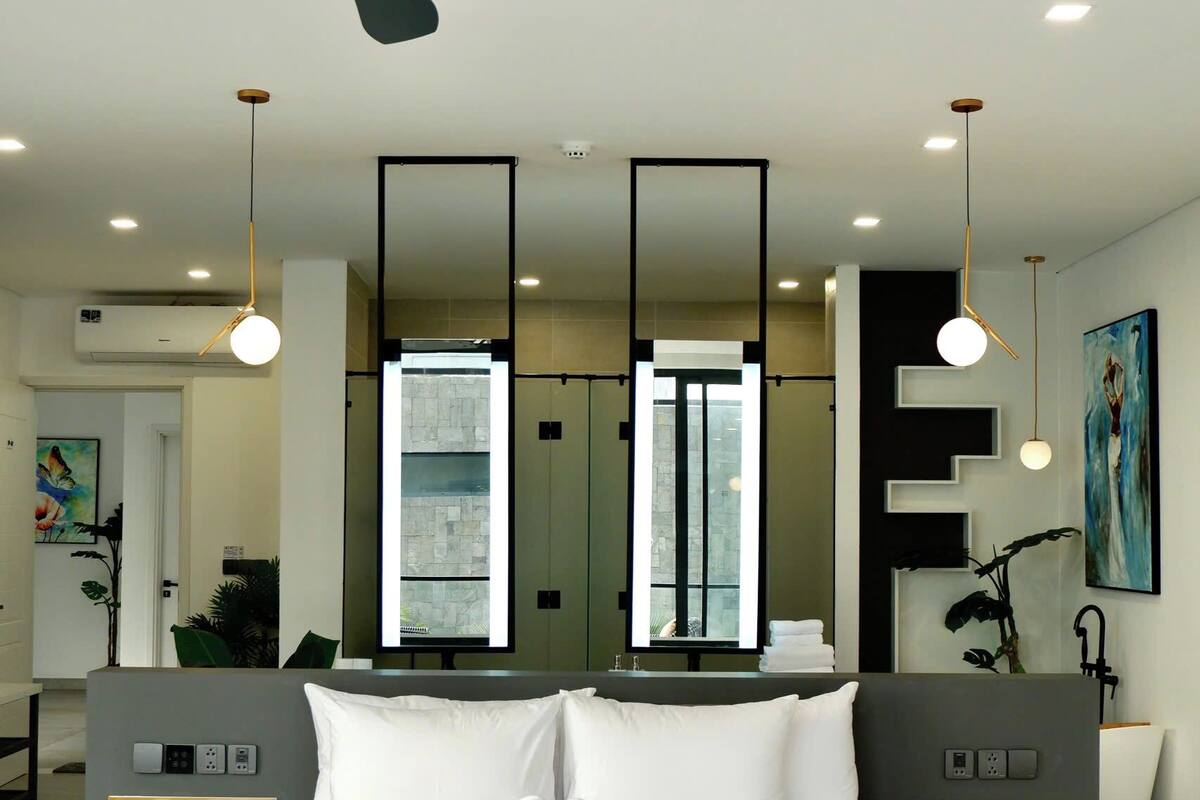 Quarto de hotel moderno com uma cama grande, ventilador de teto, iluminação embutida, um espelho grande e uma pintura na parede.