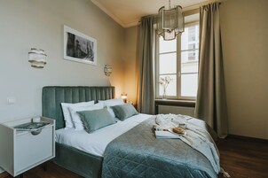 Quarto bem arrumado com cama, mesa de cabeceira e janela com cortinas.