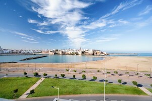 Paisagem costeira com uma fortaleza imponente, uma praia de areia e um céu azul límpido.