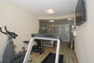 Uma academia com equipamentos de ginástica, esteira e televisão na parede.