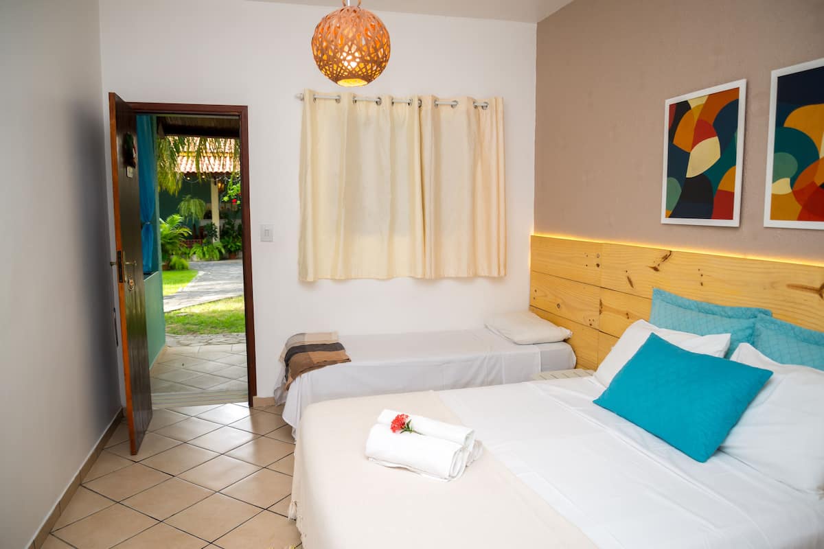 Quarto de hotel com duas camas, cabeceira de madeira, cortina e luminária pendente.