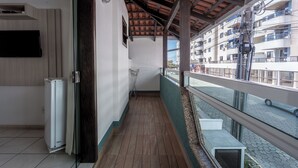 Uma varanda estreita com chão de azulejos, uma geladeira branca e uma porta de madeira.