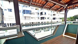Varanda com vista para um edifício alto, soalho de madeira e grades de metal.