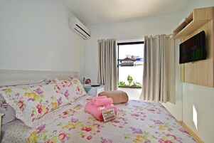 Quarto de hotel com cama, televisão, escrivaninha e janela com cortinas.