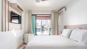 Quarto de hotel com uma cama, televisão na parede, janela com cortinas e aparelho de ar condicionado.
