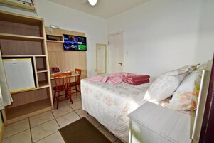 Quarto com cama, escrivaninha, cadeira, televisão e guarda-roupa.