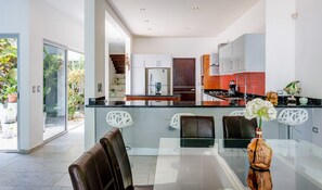 Cozinha moderna com área de jantar em vidro, armários brancos e painel de parede vermelho.
