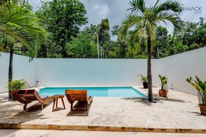 Uma área de piscina com espreguiçadeiras de madeira e plantas em vasos.