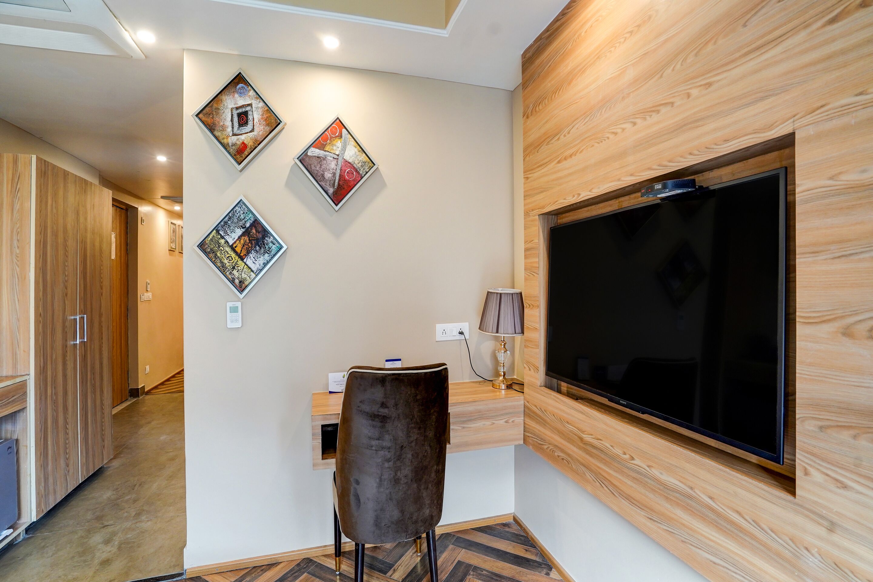Quarto moderno com painel de parede em madeira, uma televisão de tela plana grande, uma escrivaninha com cadeira e duas obras de arte abstratas na parede.