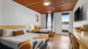 Quarto de hotel com duas camas, televisão, escrivaninha e vista para o exterior.