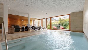 Piscina interior com espreguiçadeiras e vista para uma paisagem montanhosa através de grandes janelas.