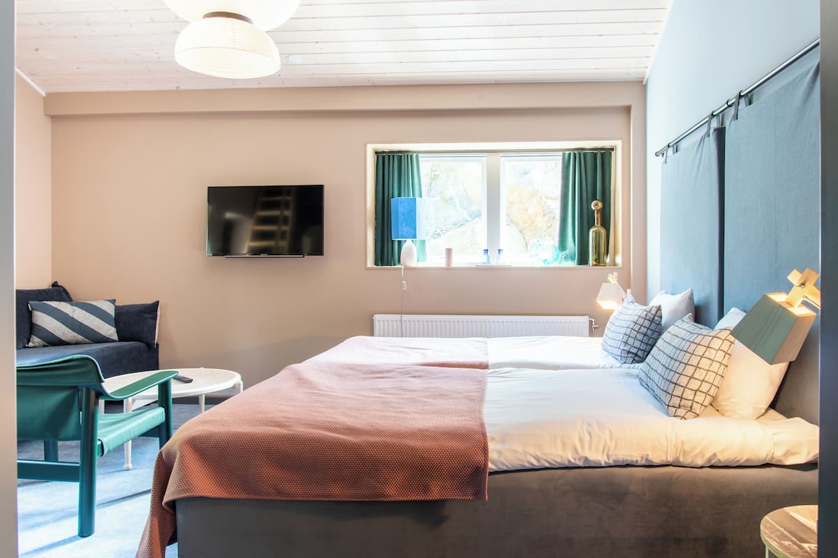 Quarto de hotel com cama, televisão, janela com cortinas, uma cadeira e uma mesa.