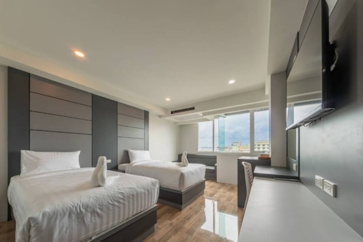 Quarto de hotel moderno com duas camas, uma escrivaninha e uma janela grande com vista para a cidade.