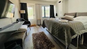 Quarto de hotel moderno com cama, escrivaninha, cadeira e televisão fixada na parede.