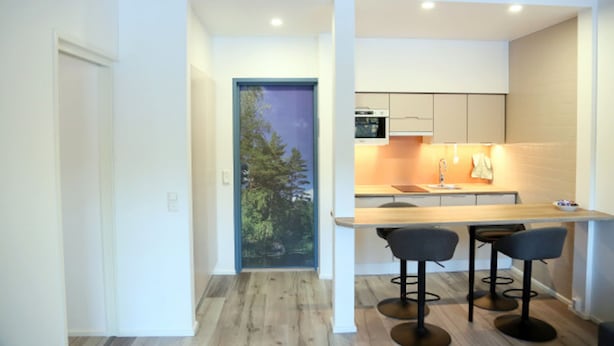 Cozinha moderna com bancada de madeira, dois bancos altos e vista para árvores através de uma porta.