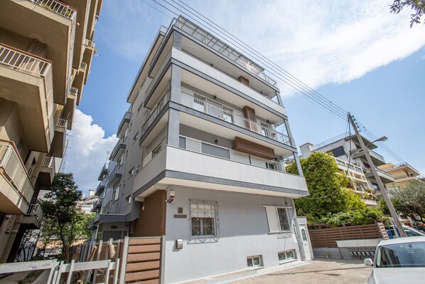Um edifício residencial de vários andares com varandas, entrada com portão e uma árvore no pátio.