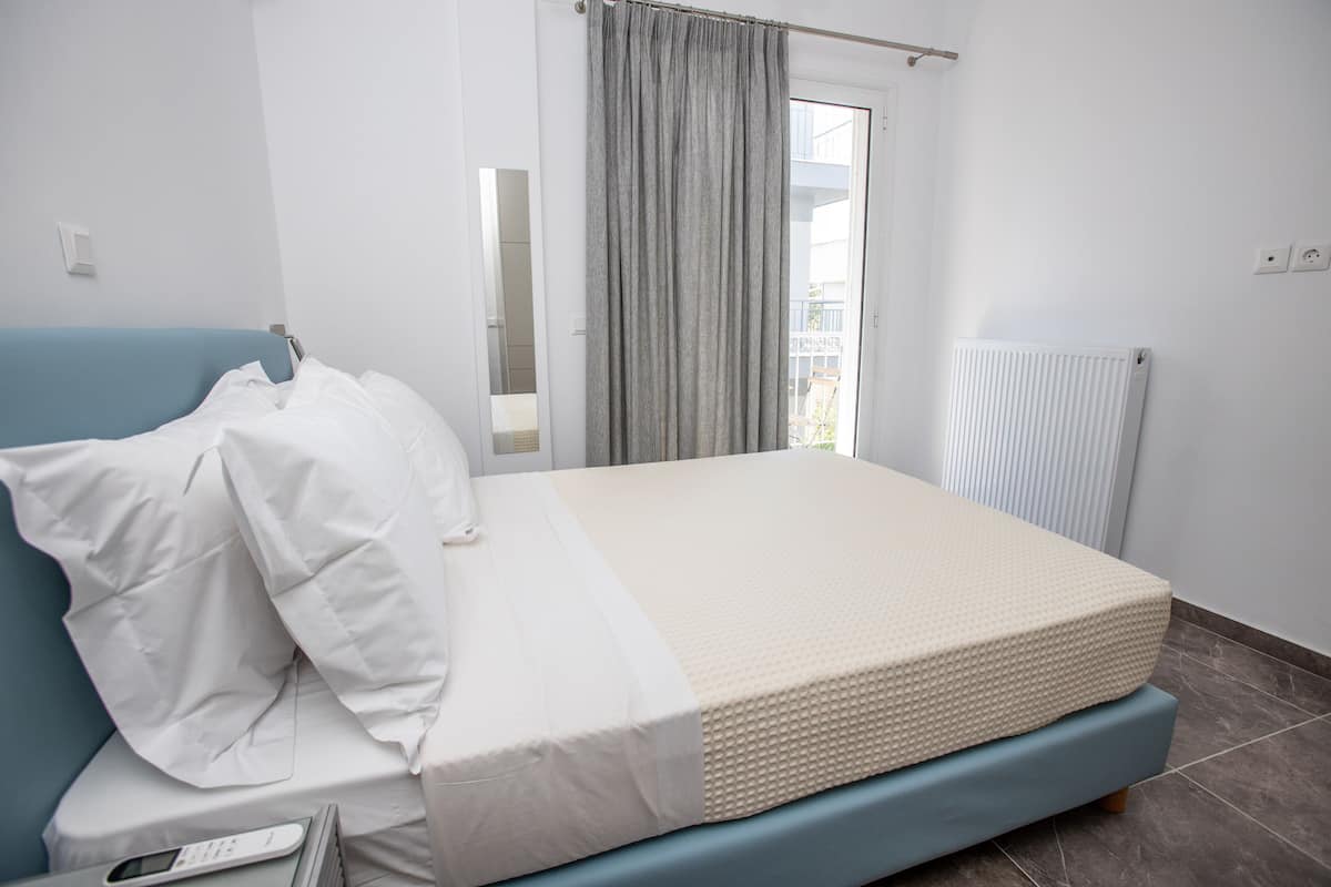 Uma cama bem arrumada com roupa de cama branca e bege, um cabeceiro azul e uma mesa de cabeceira com um controle remoto.