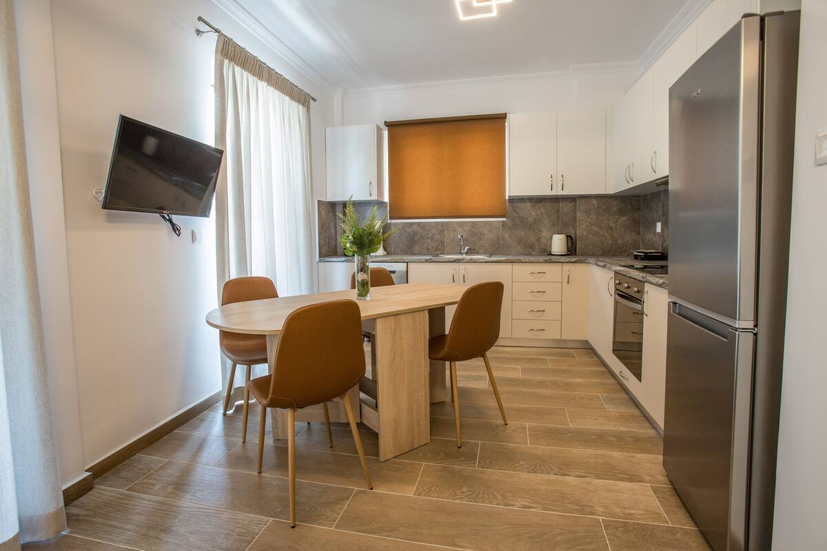 Cozinha moderna com área de refeições, incluindo mesa de madeira, cadeiras e televisão de tela plana fixada na parede.