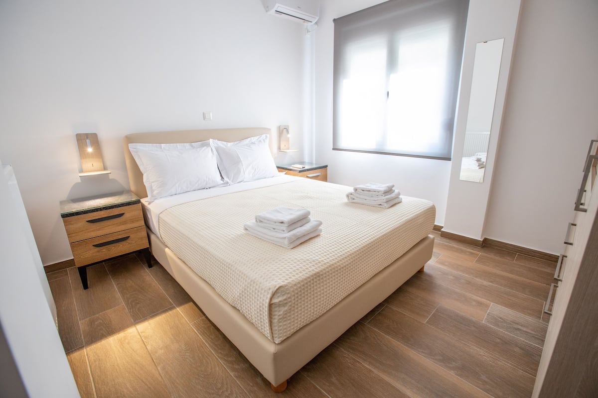 Quarto moderno com uma cama grande, piso de madeira e janela com persianas.