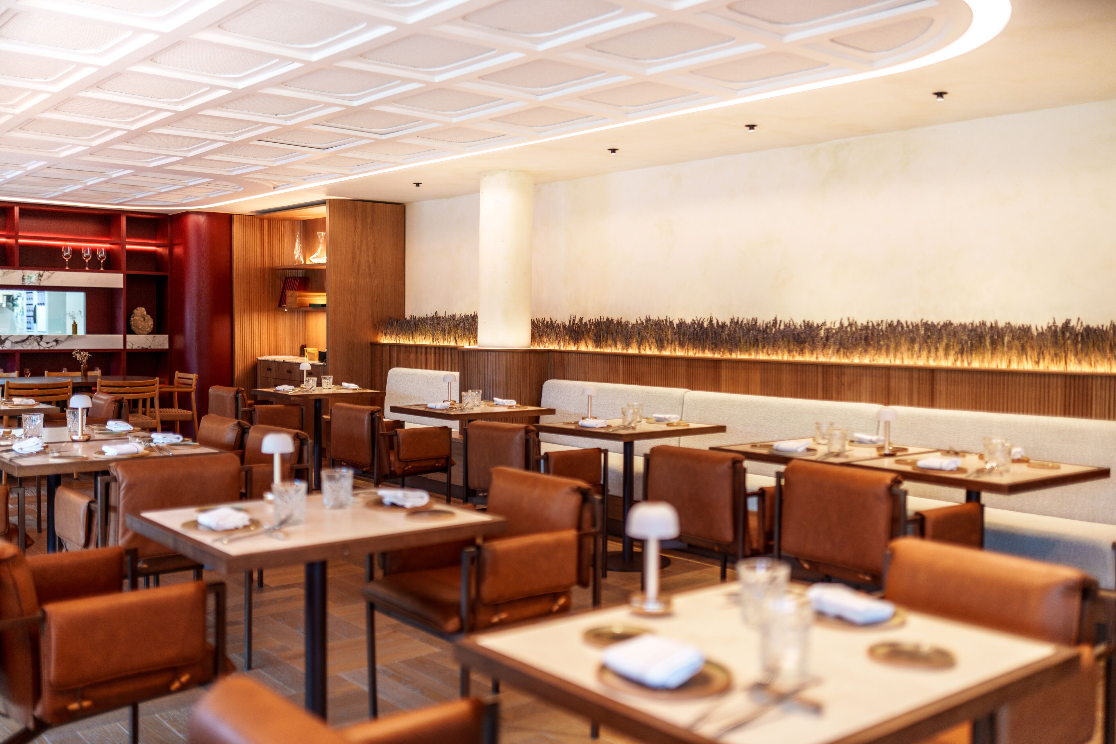 Restaurante moderno com diversas opções de assento, incluindo mesas e cabines, parede decorativa com padrão texturizado e teto com design geométrico.