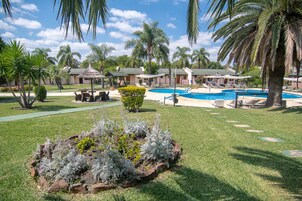 Um resort com piscina, palmeiras e áreas de descanso.