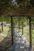 Uma galeria coberta com um caminho de concreto, cercada por árvores e uma área gramada com assentos externos.