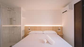 Quarto de hotel moderno com uma cama grande, área de chuveiro e cabeceira de madeira.
