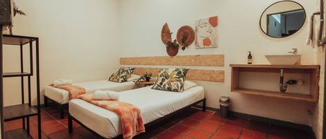 Quarto de hotel com duas camas, pia, espelho e lixeira.