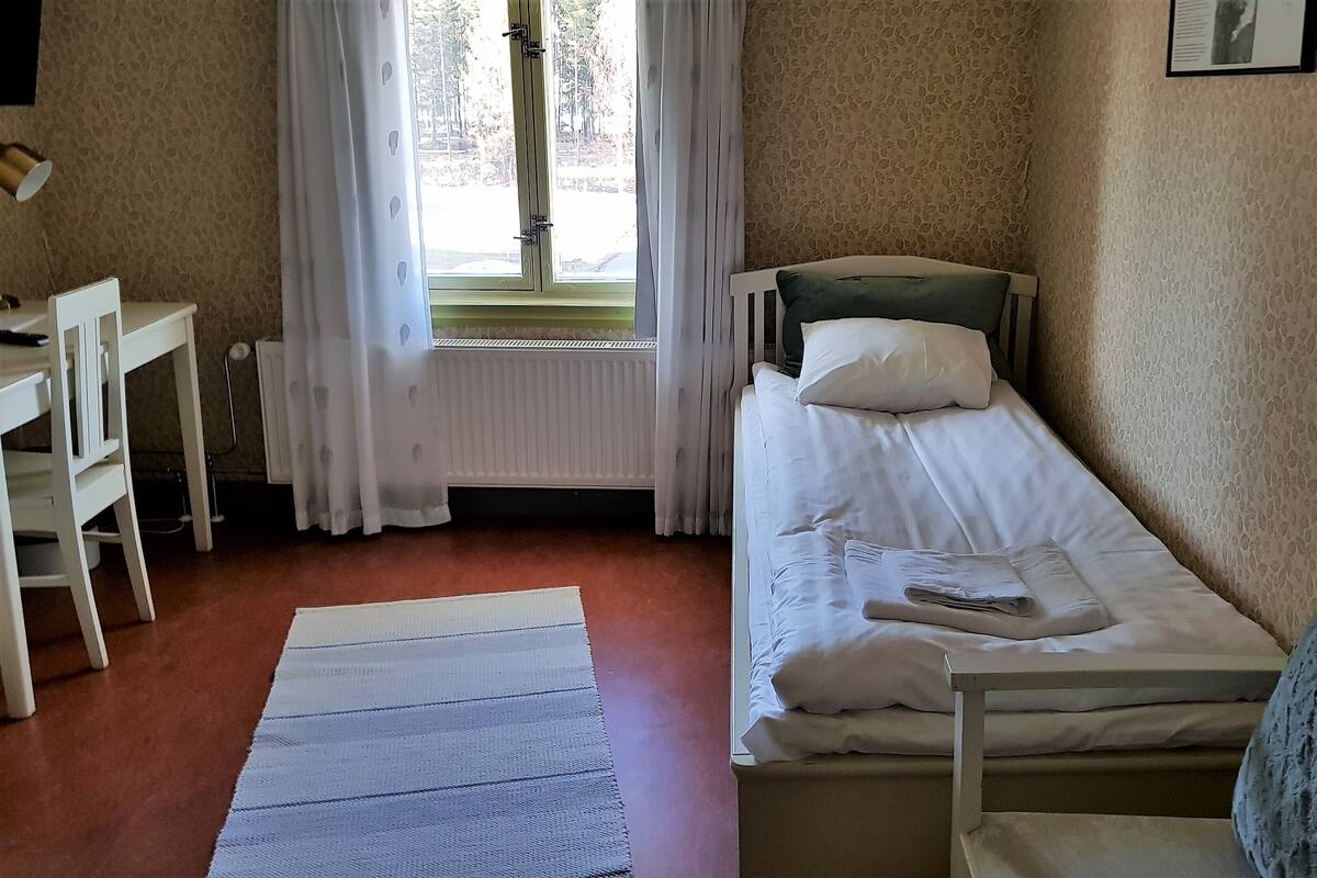 Um quarto pequeno e bem arrumado, com uma cama, uma escrivaninha e uma cadeira.