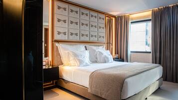 Quarto de hotel com uma cama grande, cabeceira com desenhos de borboletas, mesa de cabeceira e uma janela com cortinas.