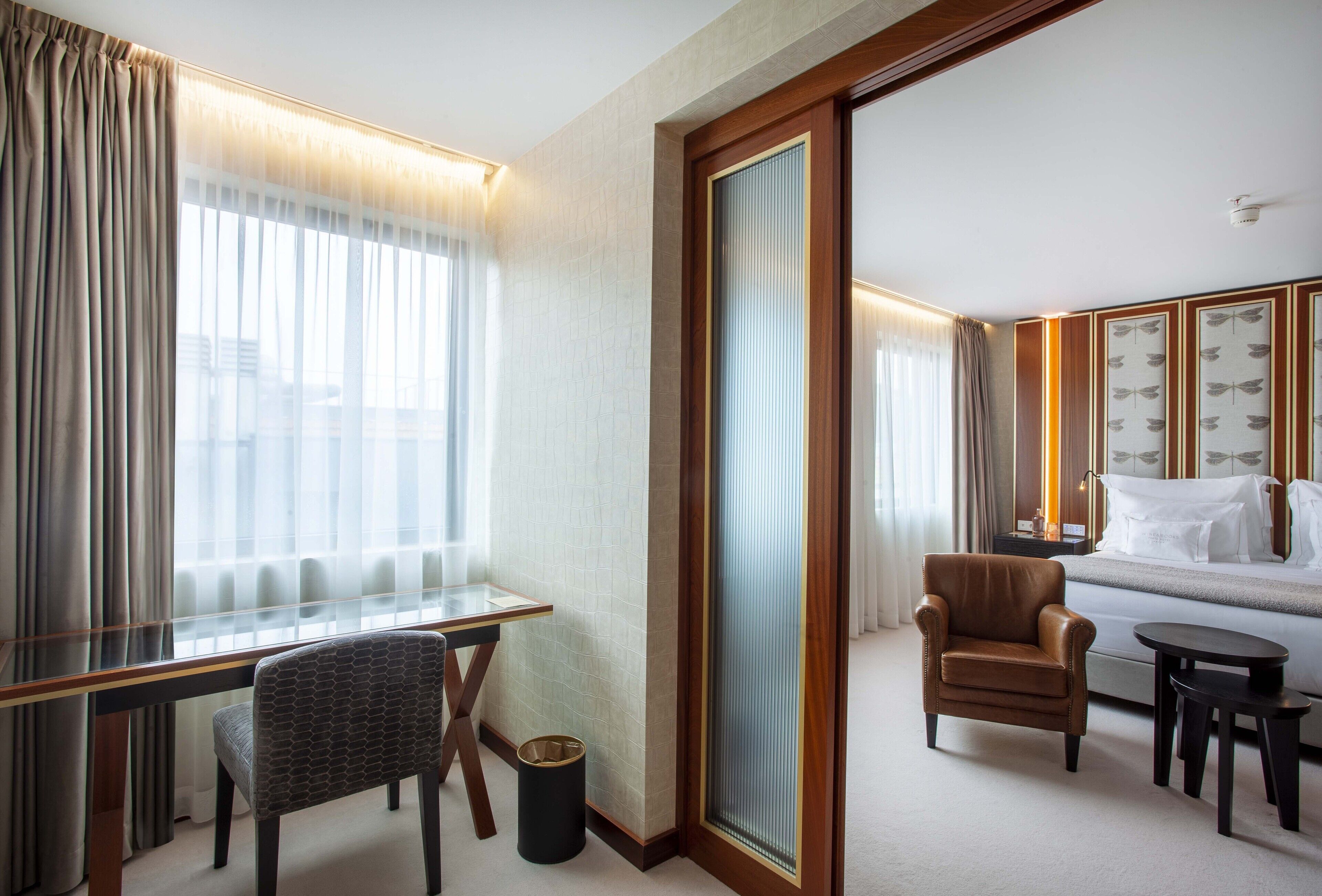 Quarto de hotel com uma cama, uma escrivaninha, uma cadeira e uma pequena mesa.