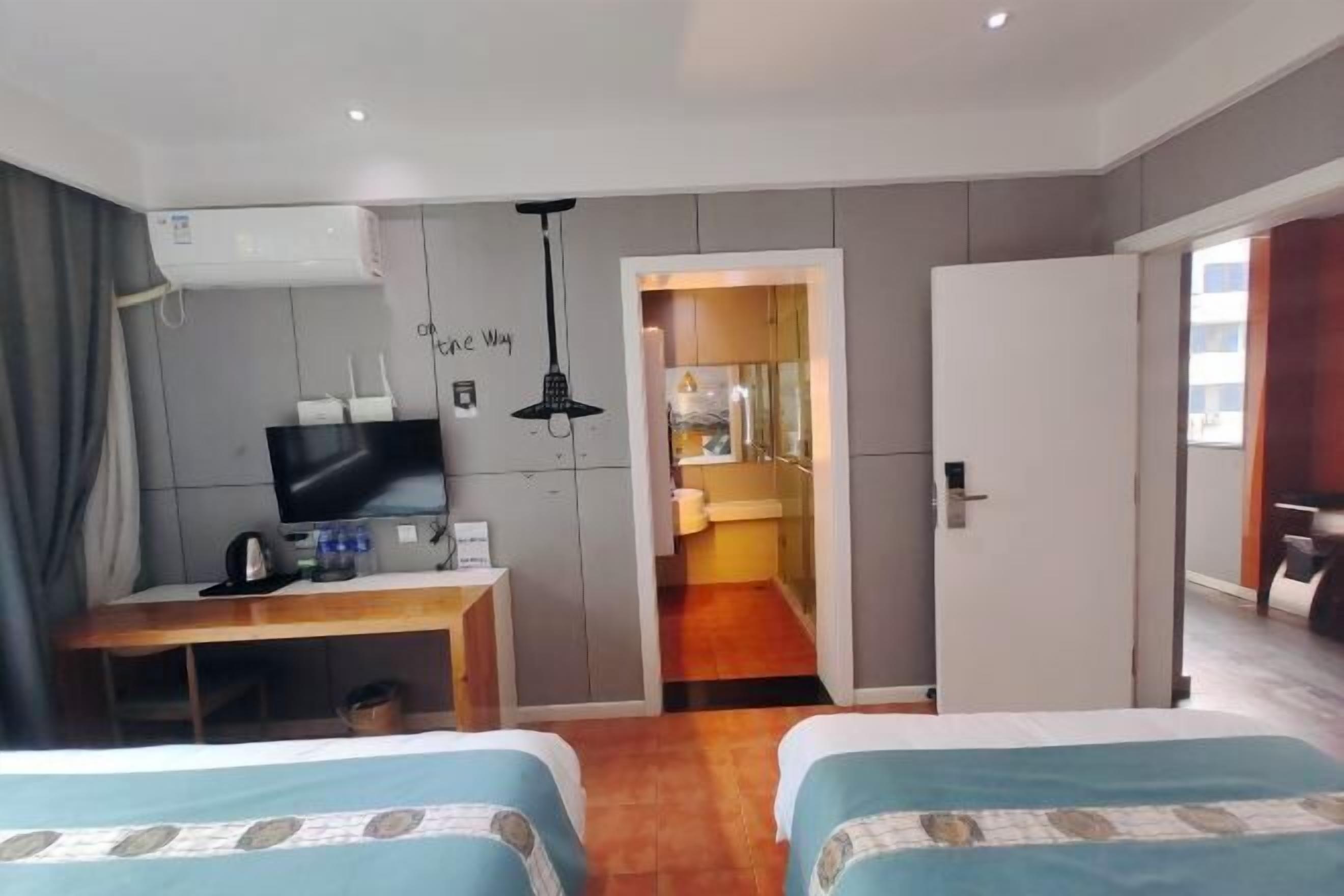 Quarto de hotel com duas camas, uma mesa, televisão, aparelho de ar condicionado e banheiro visível através de uma porta aberta.