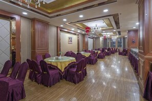 Uma sala de banquetes com mesas redondas e cadeiras de cor roxa, piso de madeira e um candelabro.