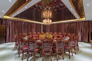 Uma sala de jantar formal com uma grande mesa redonda, várias cadeiras e um lustre.