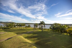 Um campo de golfe com um lago, palmeiras e céu claro.