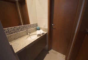 Casa de banho com bancada de granito, pia e espelho. Há toalhas na bancada e um vaso azul.