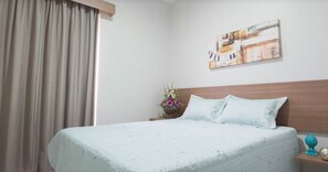Quarto de hotel com cama, mesa de cabeceira, um vaso com flores e um quadro na parede.
