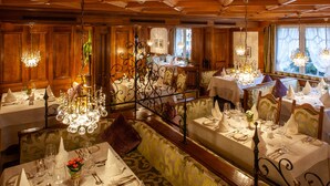 Um restaurante com painéis de madeira, lustres elaborados e uma área de estar acolhedora com estofados estampados.