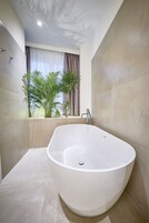 Um banheiro moderno com uma banheira independente, uma janela com cortinas e plantas em vasos.