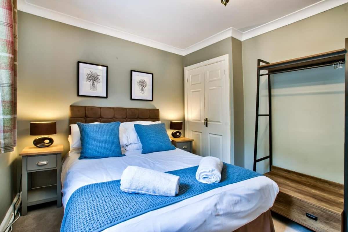 Quarto bem arrumado com uma cama, duas mesas de cabeceira, um guarda-roupa e duas fotos emolduradas na parede.