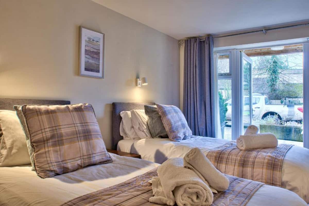 Quarto de hotel com duas camas, uma janela com cortinas, um quadro na parede e vista para o exterior.